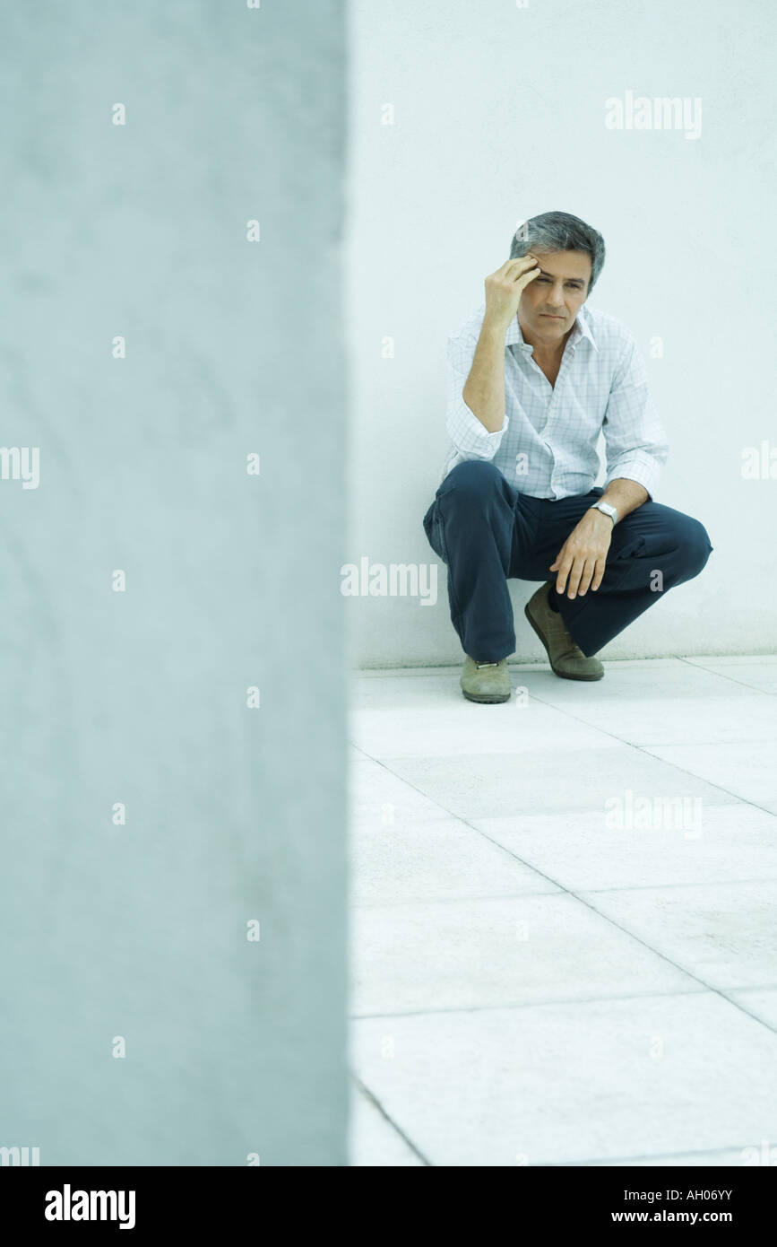 Mature man crouching, holding head, full length portrait Stock Photo ...