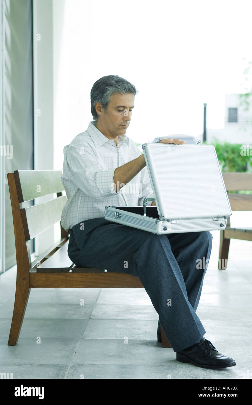 Mature man sitting on bench, opening briefcase, full length Stock Photo ...