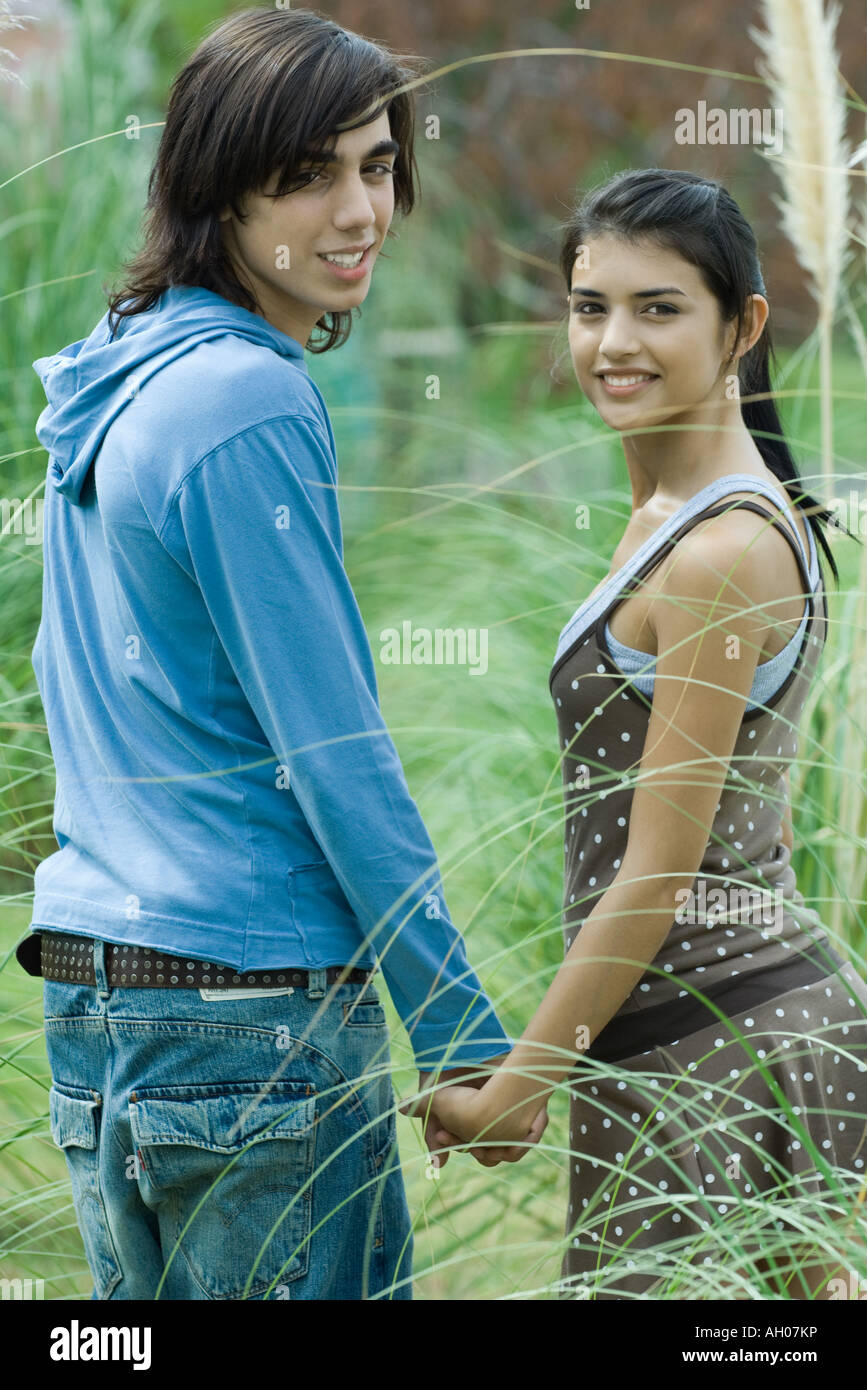 Young couple holding hands, looking over shoulders at camera Stock ...