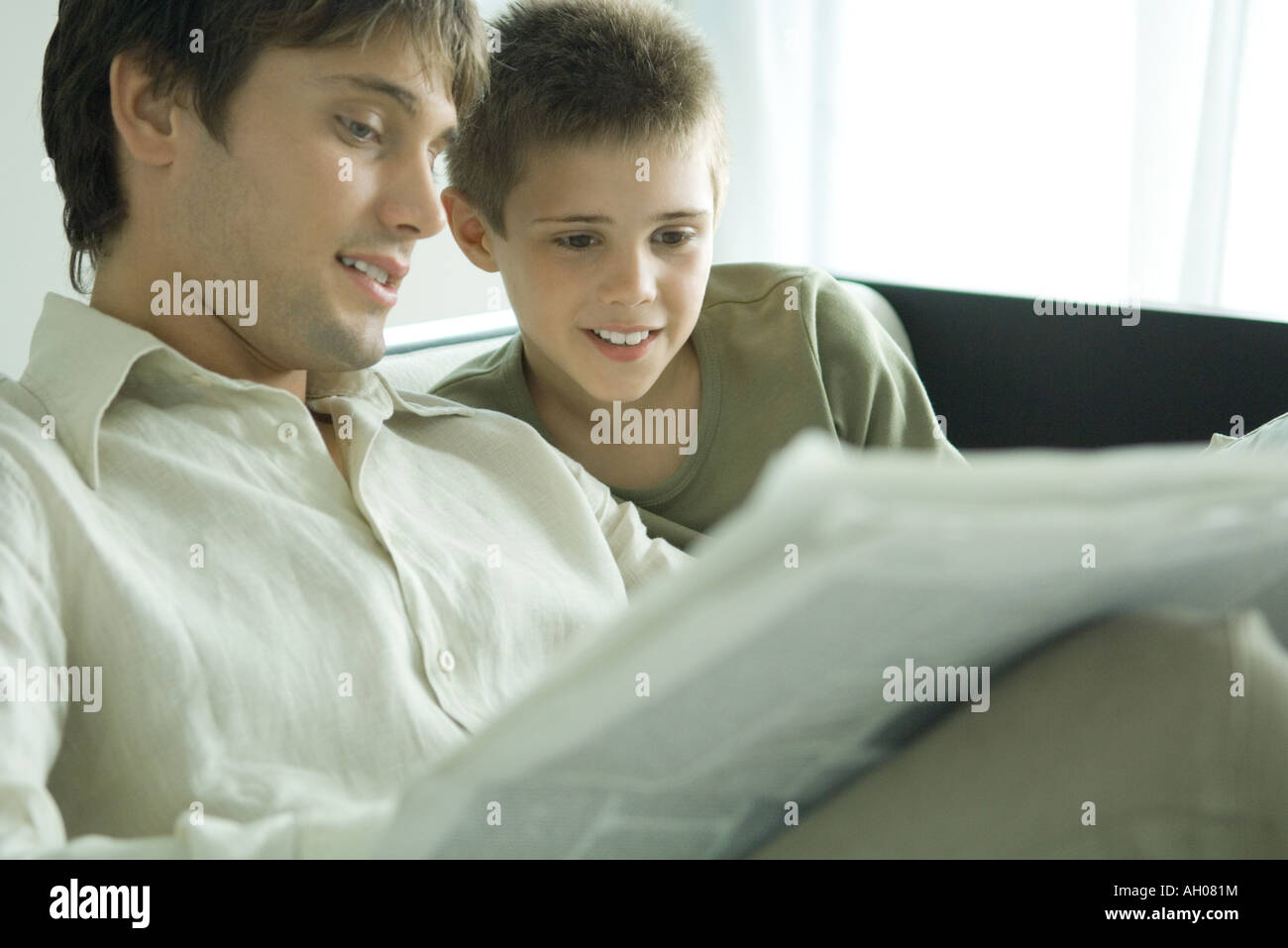 Boy and father reading newspaper together on sofa Stock Photo - Alamy