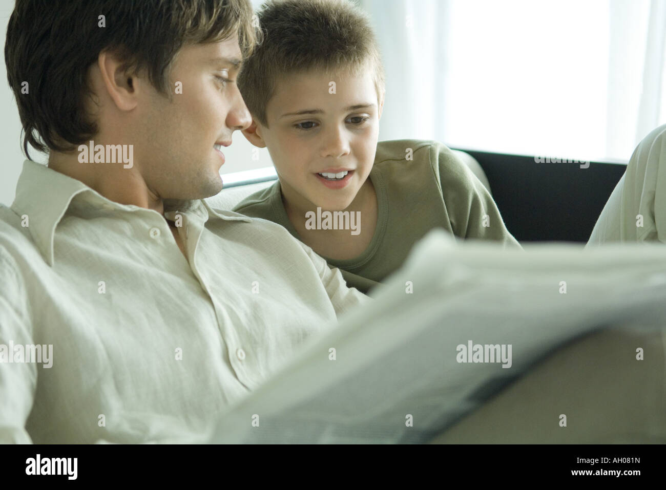 Boy and father reading newspaper together on sofa Stock Photo - Alamy