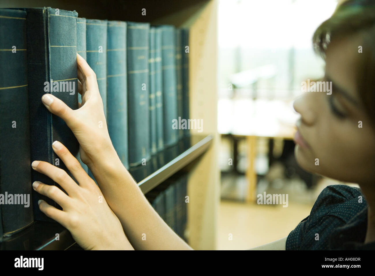 Female student taking reference book from shelf in library Stock Photo ...