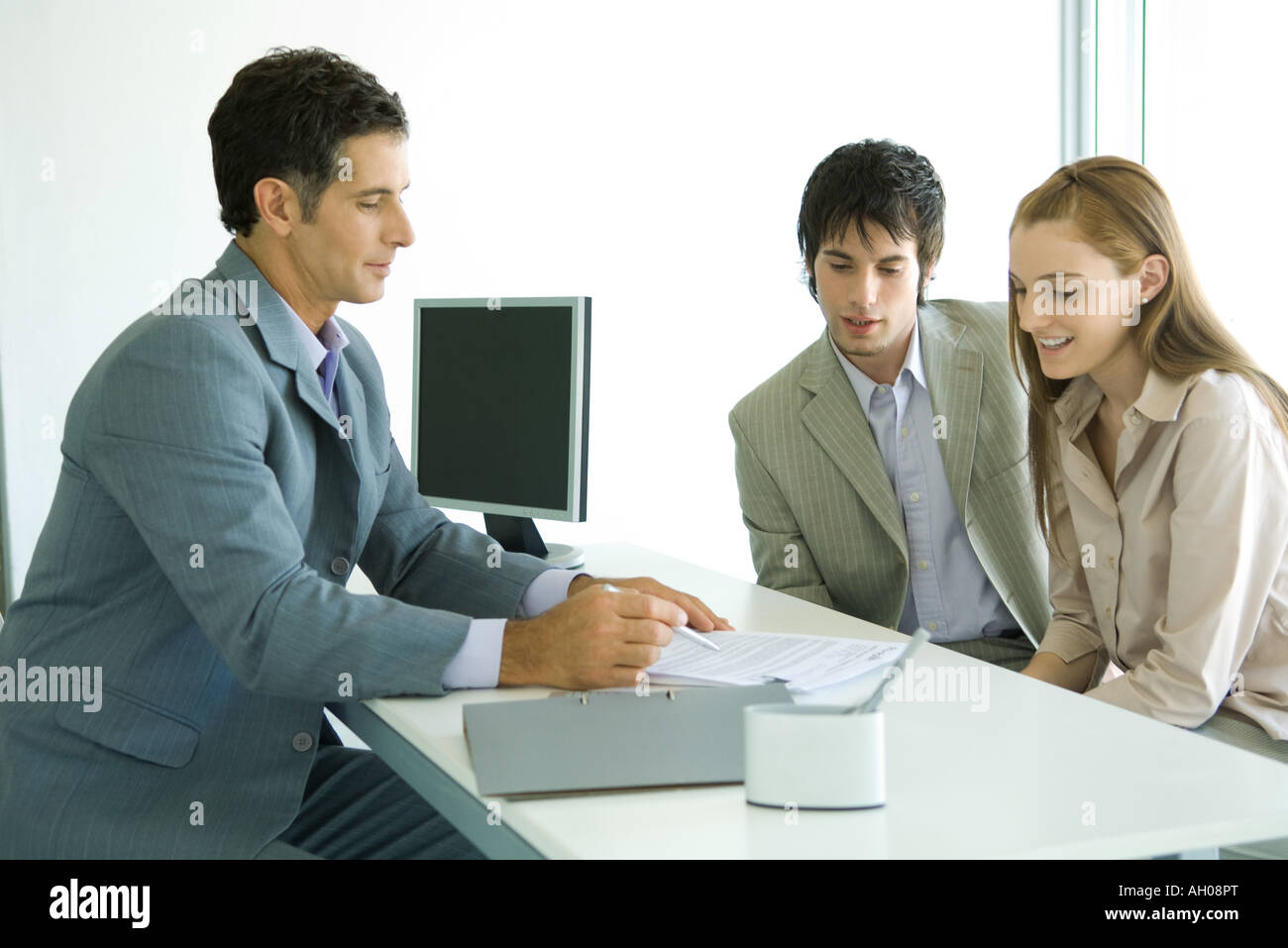 Young couple sitting across desk from businessman, businessman pointing ...