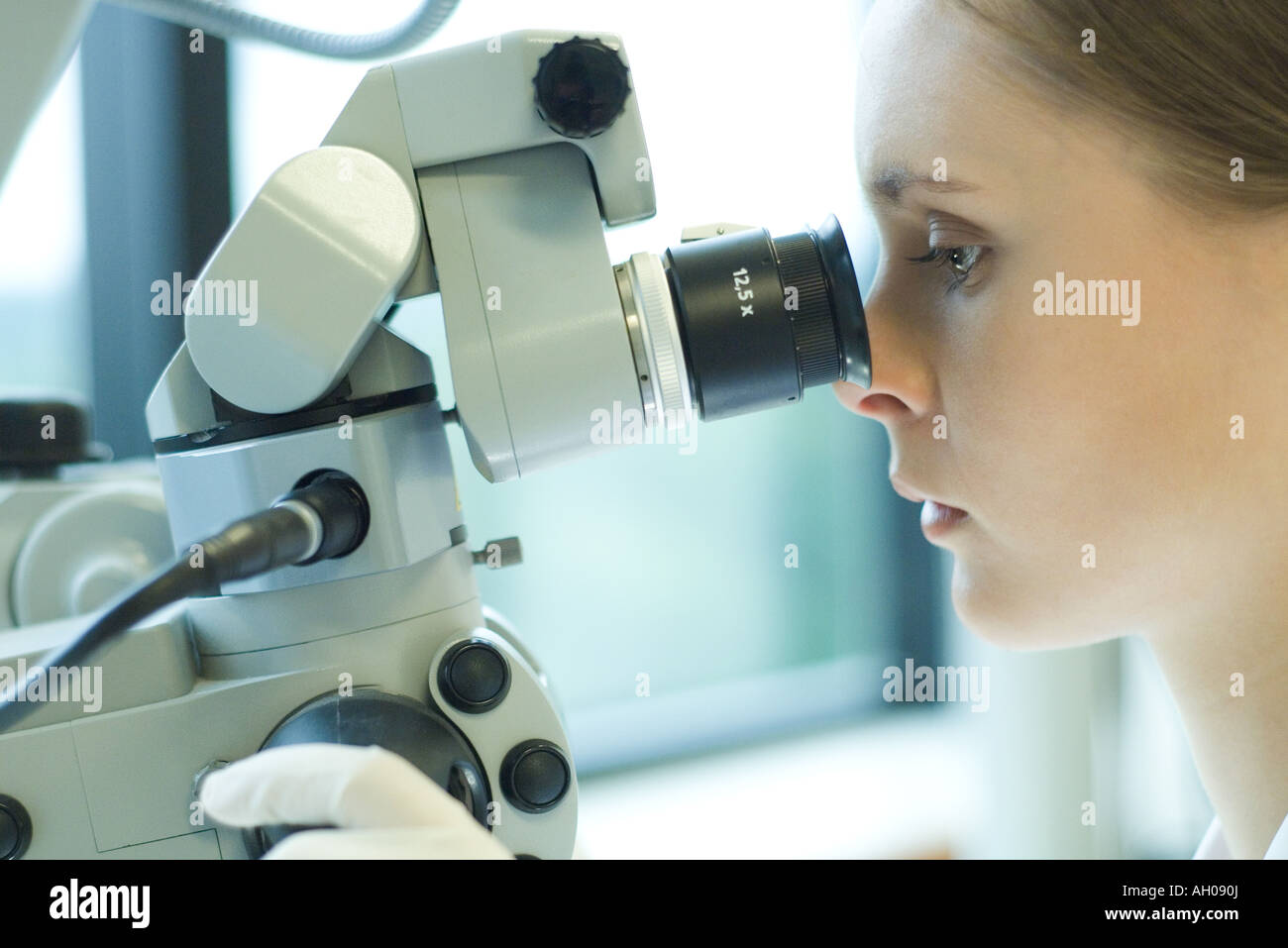 Young female scientist looking through microscope, extreme close-up ...