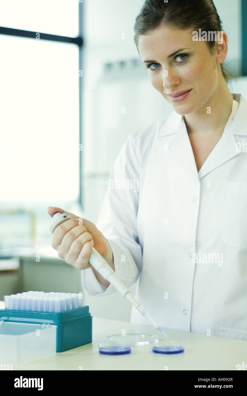 Female lab worker dropping solution into Petri dish, smiling at camera ...
