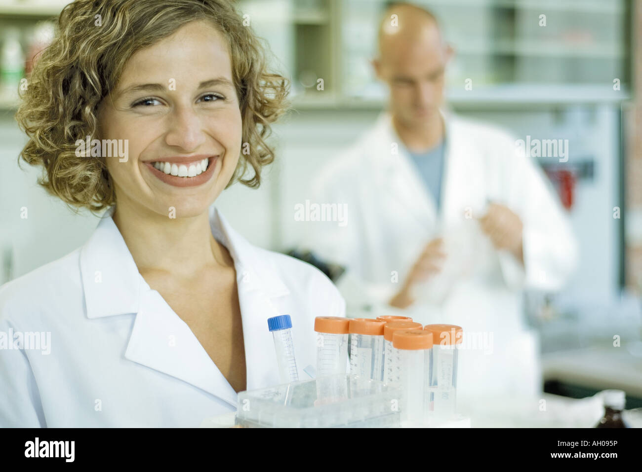 Female lab worker holding rack of empty test tubes, smiling at camera ...