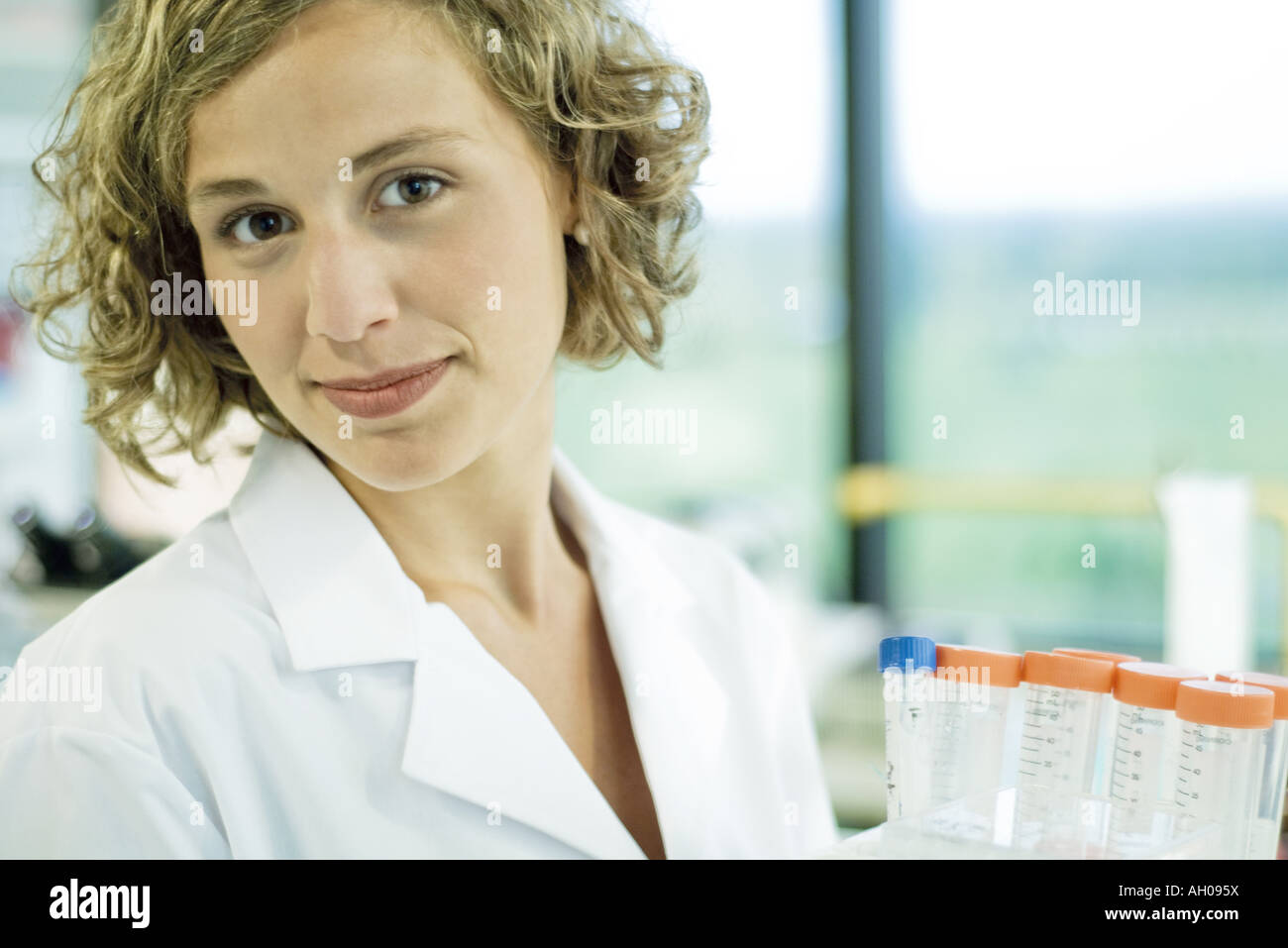 Female lab worker holding rack of empty test tubes, looking at camera ...