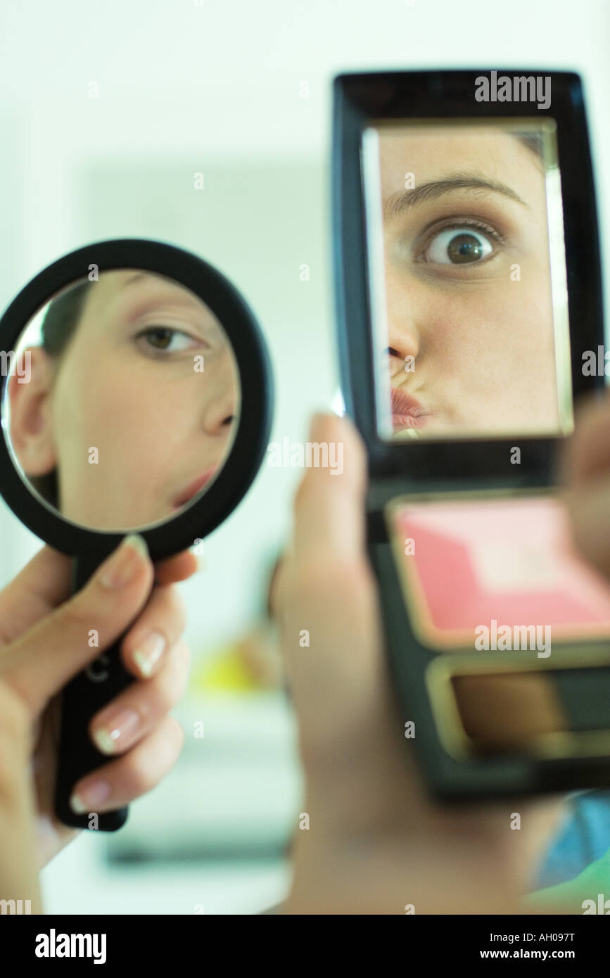 Two young friends looking at selves in hand mirrors, one making faces ...
