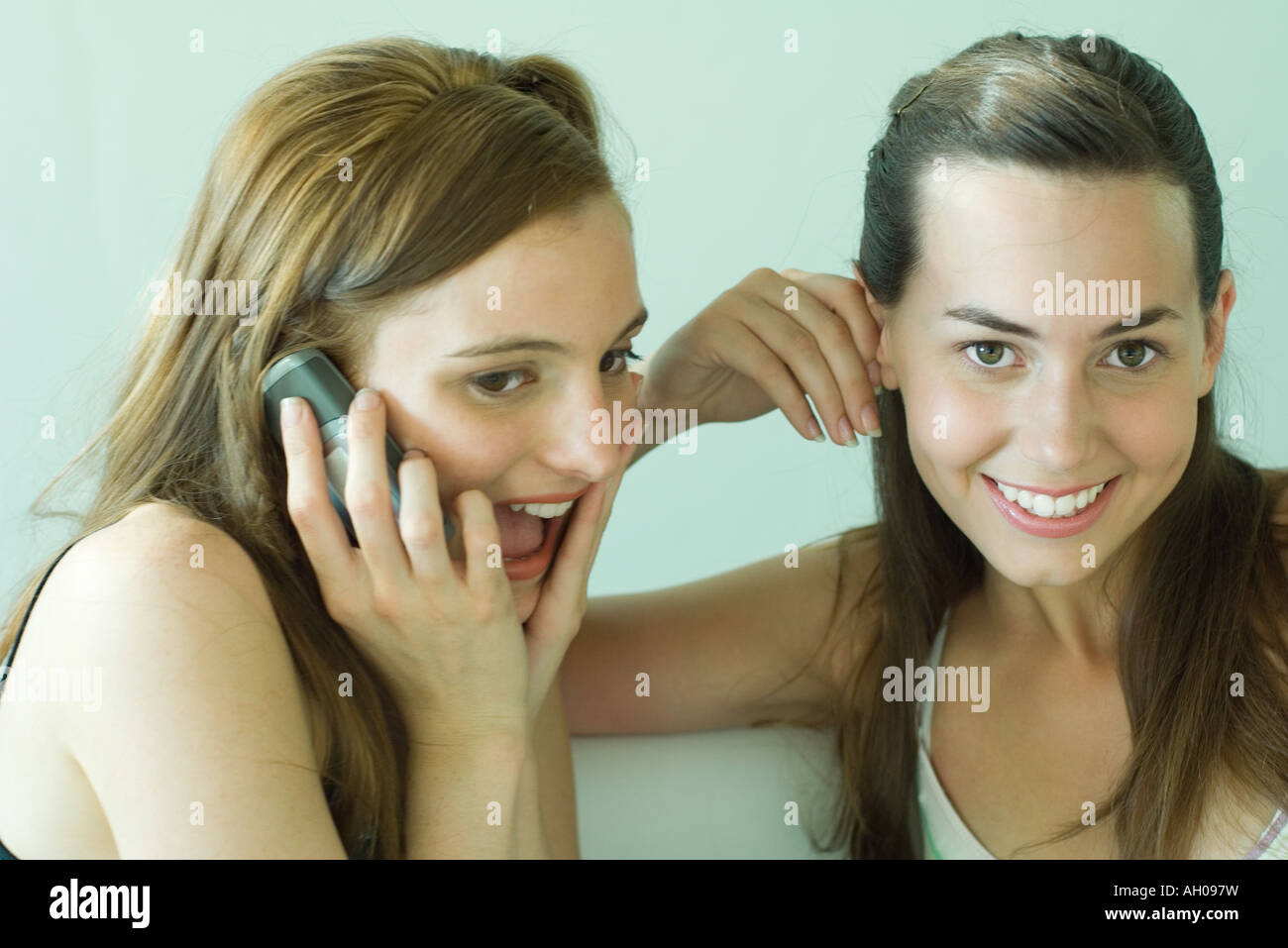 Two young friends smiling together, using cell phone, one looking at ...