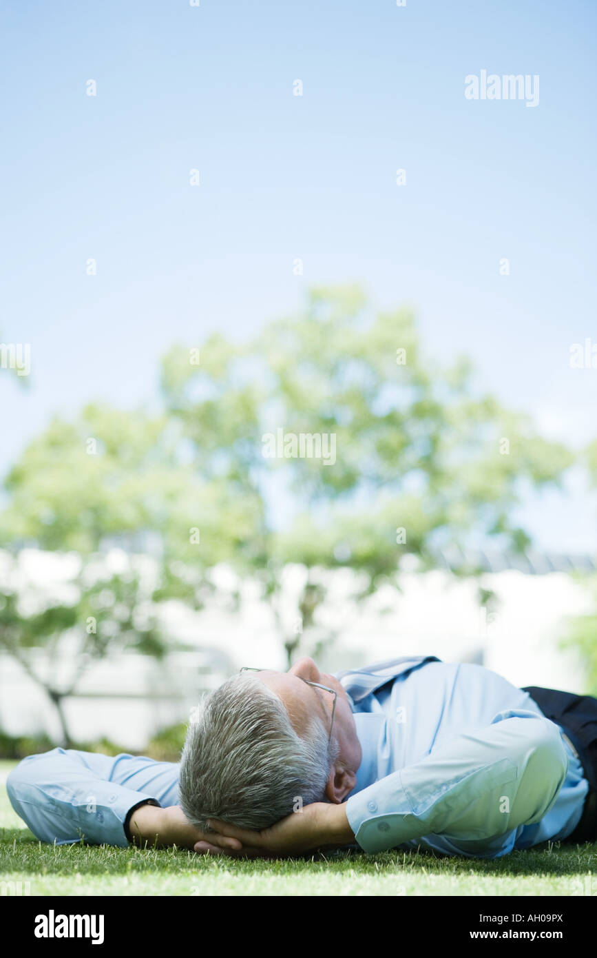 Mature businessman lying on ground outdoors, hands behind head Stock ...