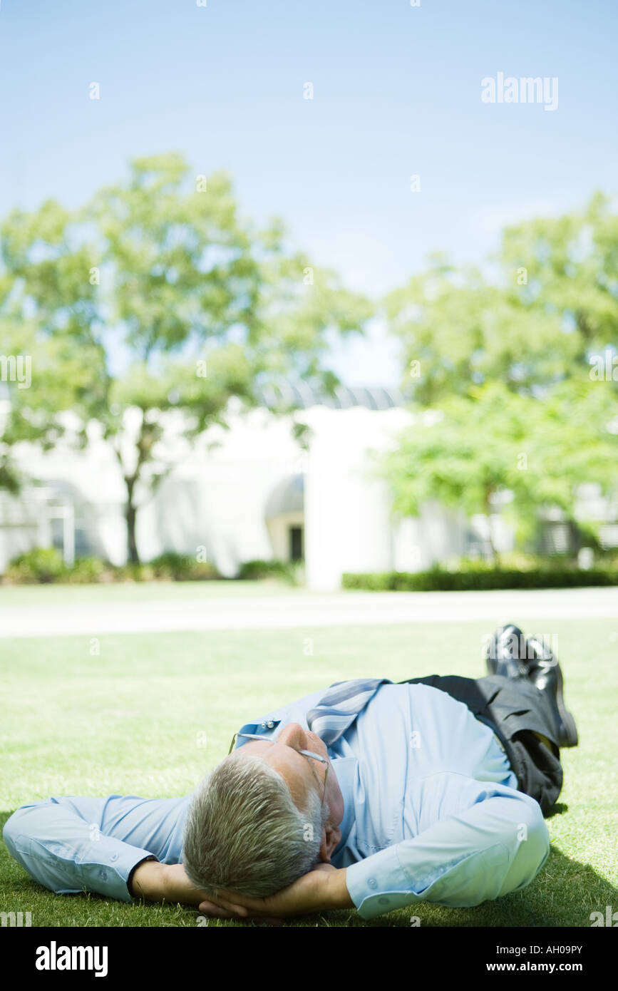 Mature businessman lying on ground outdoors, hands behind head, full ...