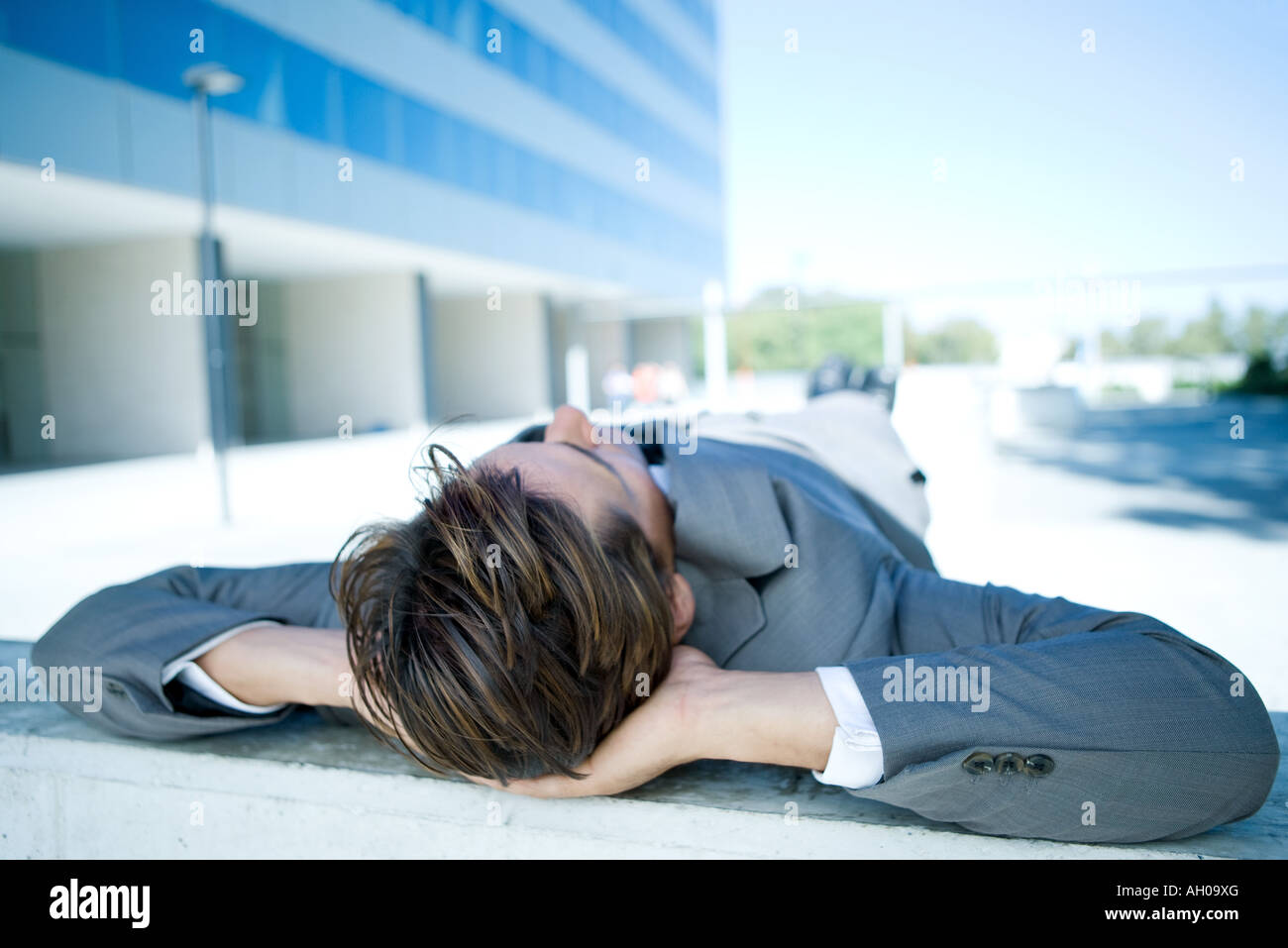 Businessman lying on ground outdoors, hands behind head, full length ...