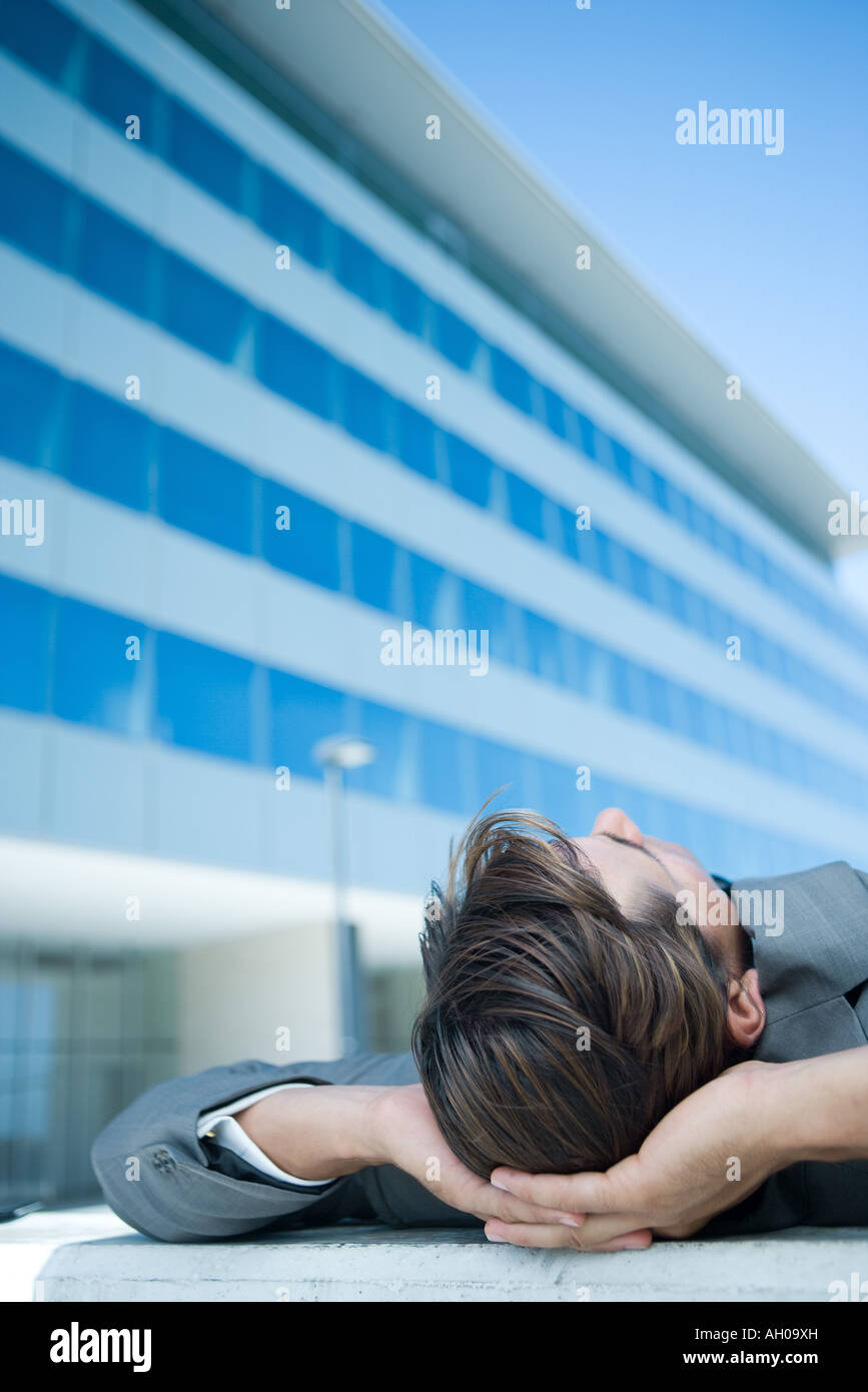 Businessman lying on ground outdoors, hands behind head, cropped view ...