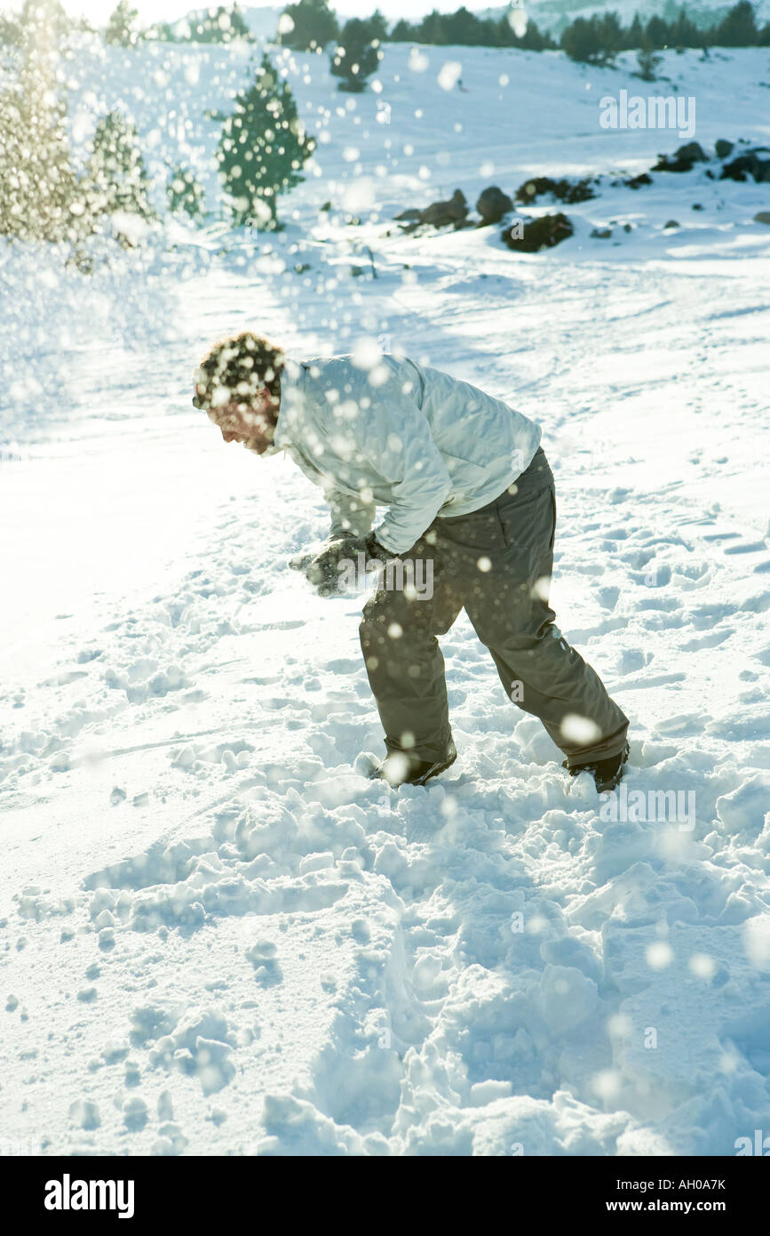 Young man bending over in snow, dodging snowball, full length Stock ...