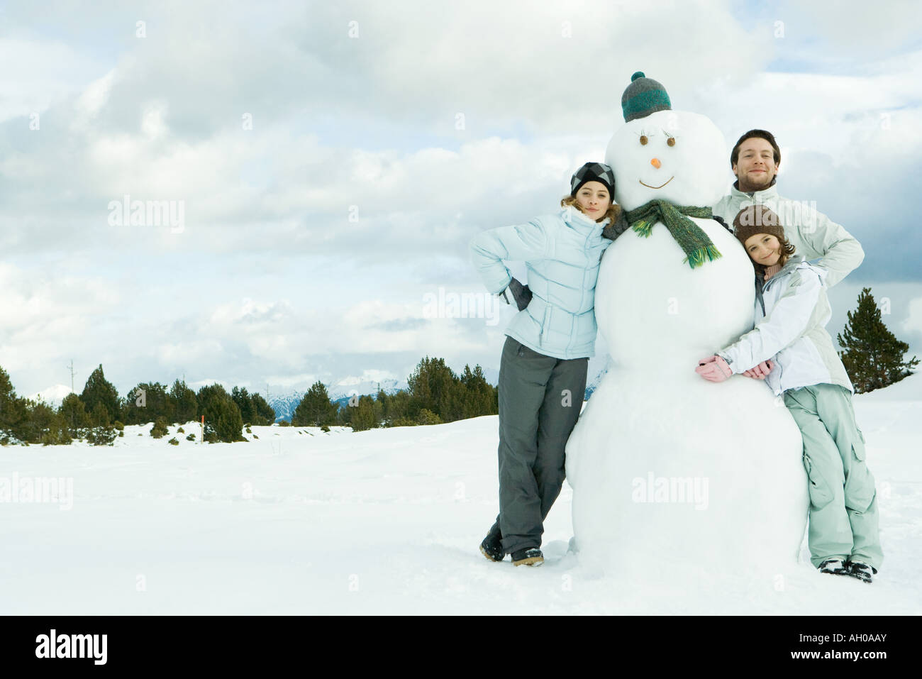Three young friends leaning against snowman, smiling at camera ...