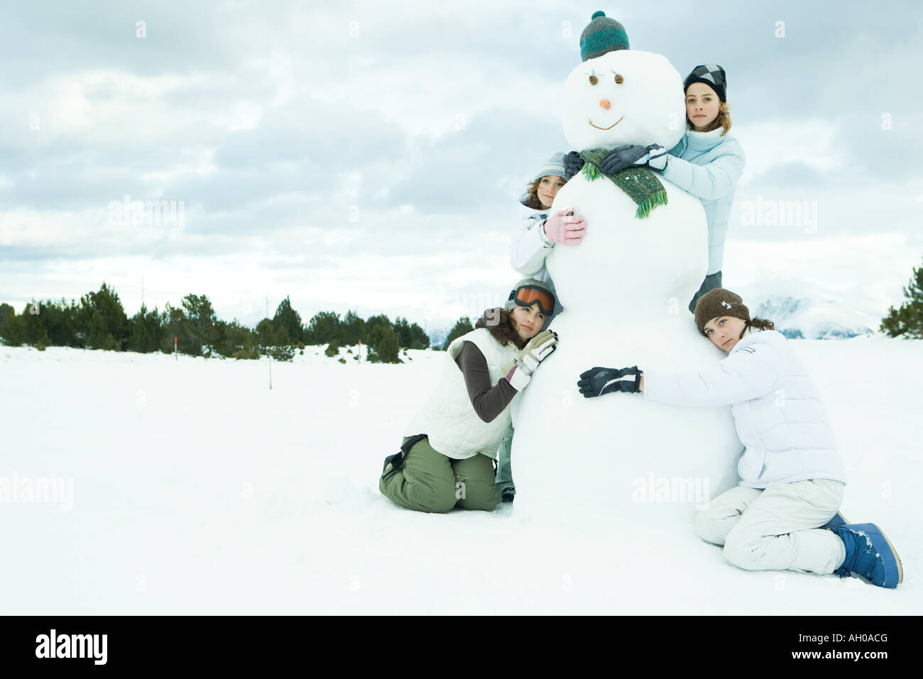 Four young friends embracing snowman, group portrait, one looking at ...
