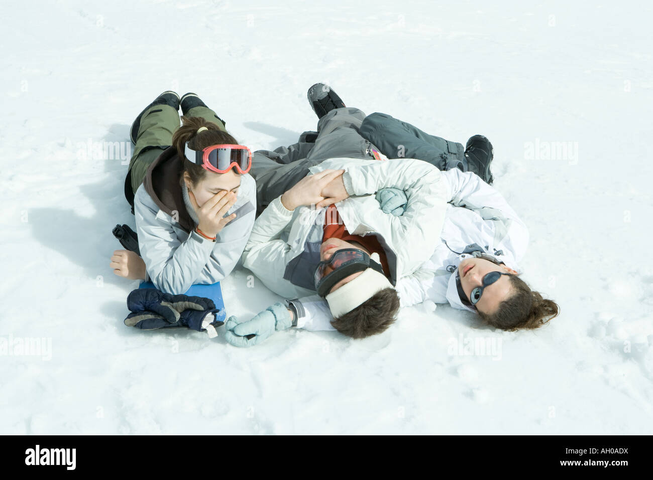 Three young friends reclining in snow, one holding head Stock Photo - Alamy