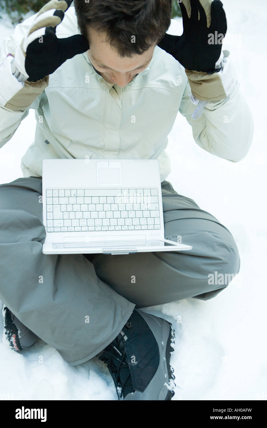 Young man sitting on the ground in snow, holding laptop computer on lap ...