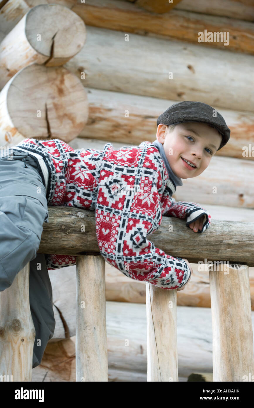 Boy climbing on rail in front of log cabin, smiling at camera Stock ...