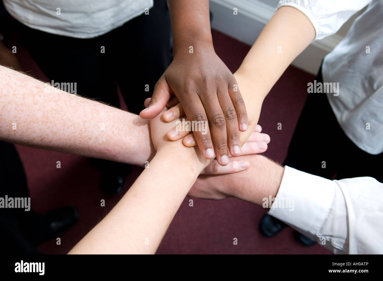 Five office workers showing team work by placing hands on top of each ...