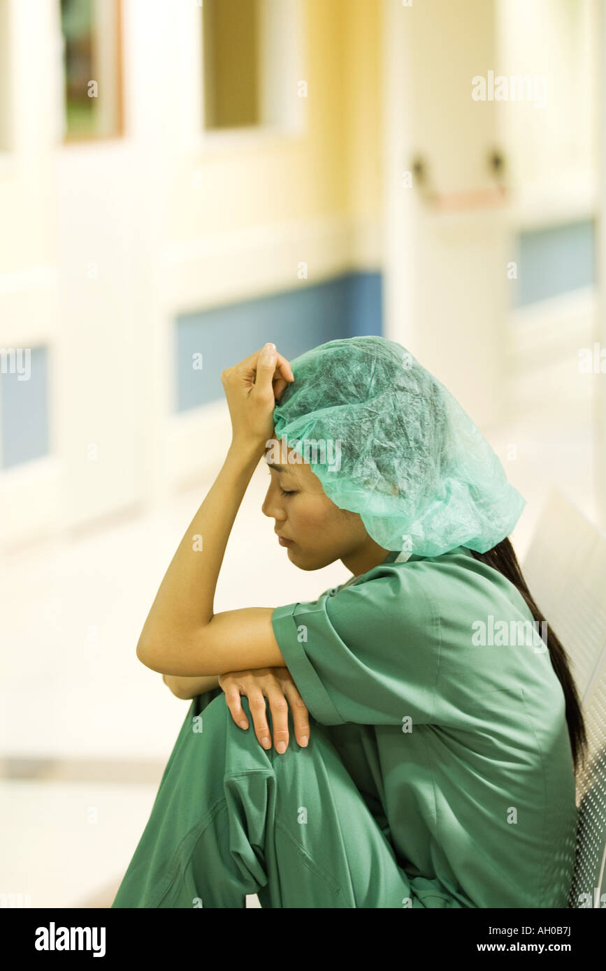 Medical worker sitting in hospital corridor, holding head, eyes closed ...