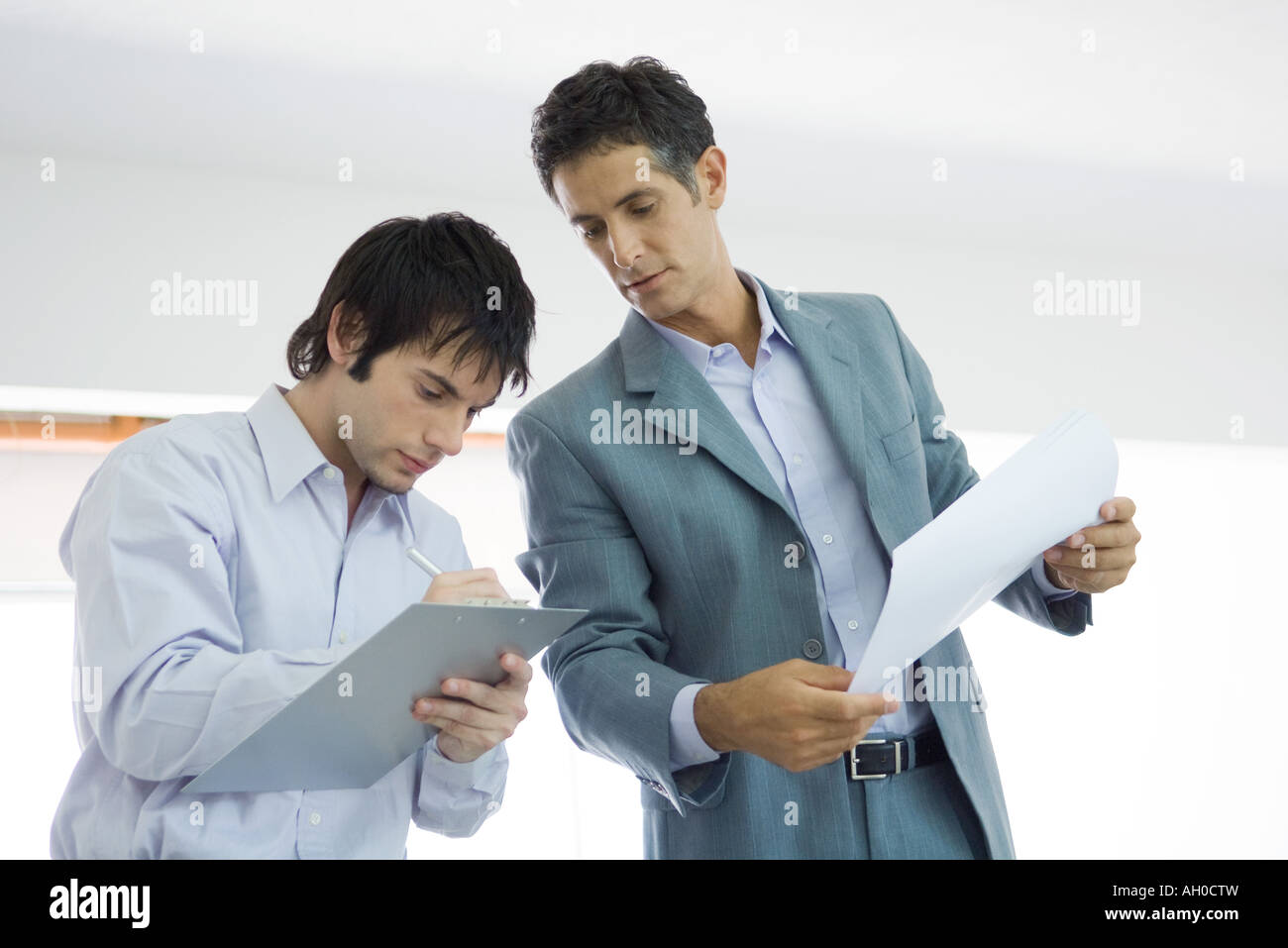 Young man writing on clipboard, mature man looking over shoulder Stock ...