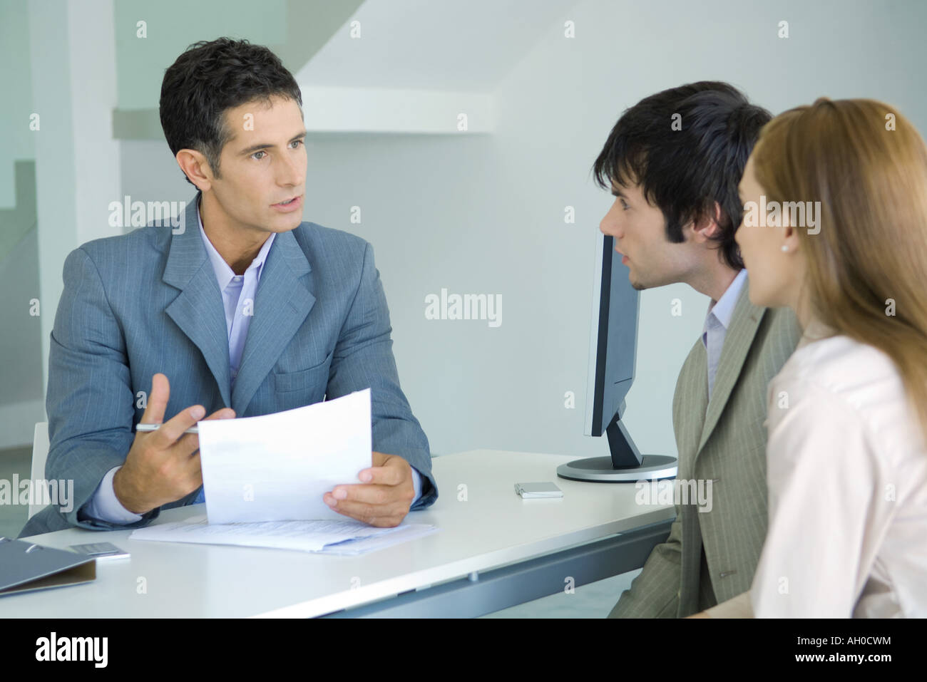 Businessman sitting across desk from young couple, holding document ...