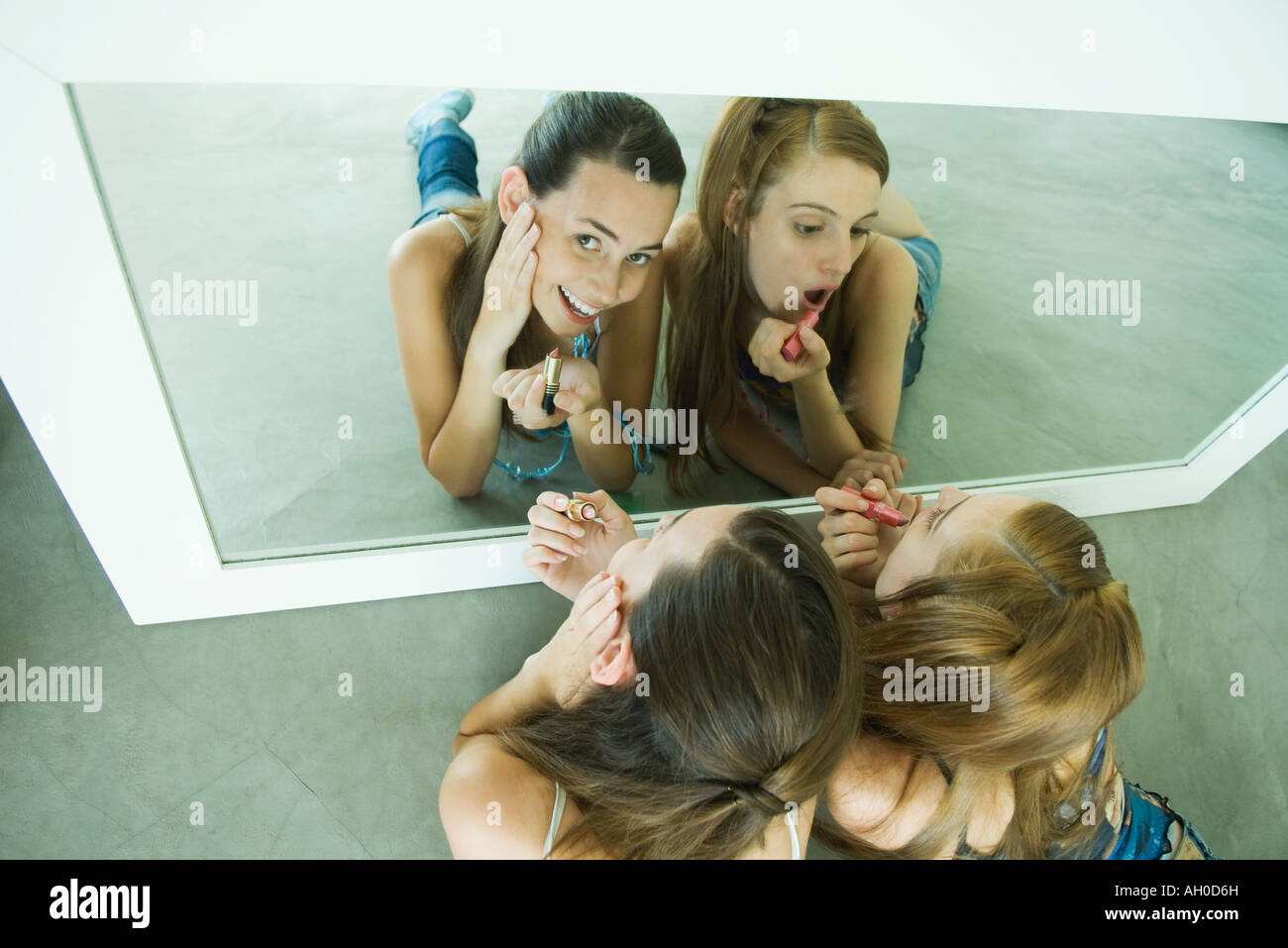 Two friends lying on ground, applying lipstick, looking in mirror, one ...