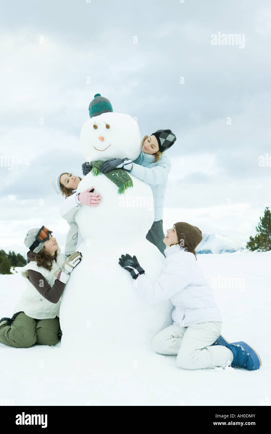 Young friends embracing snowman, smiling, full length Stock Photo - Alamy