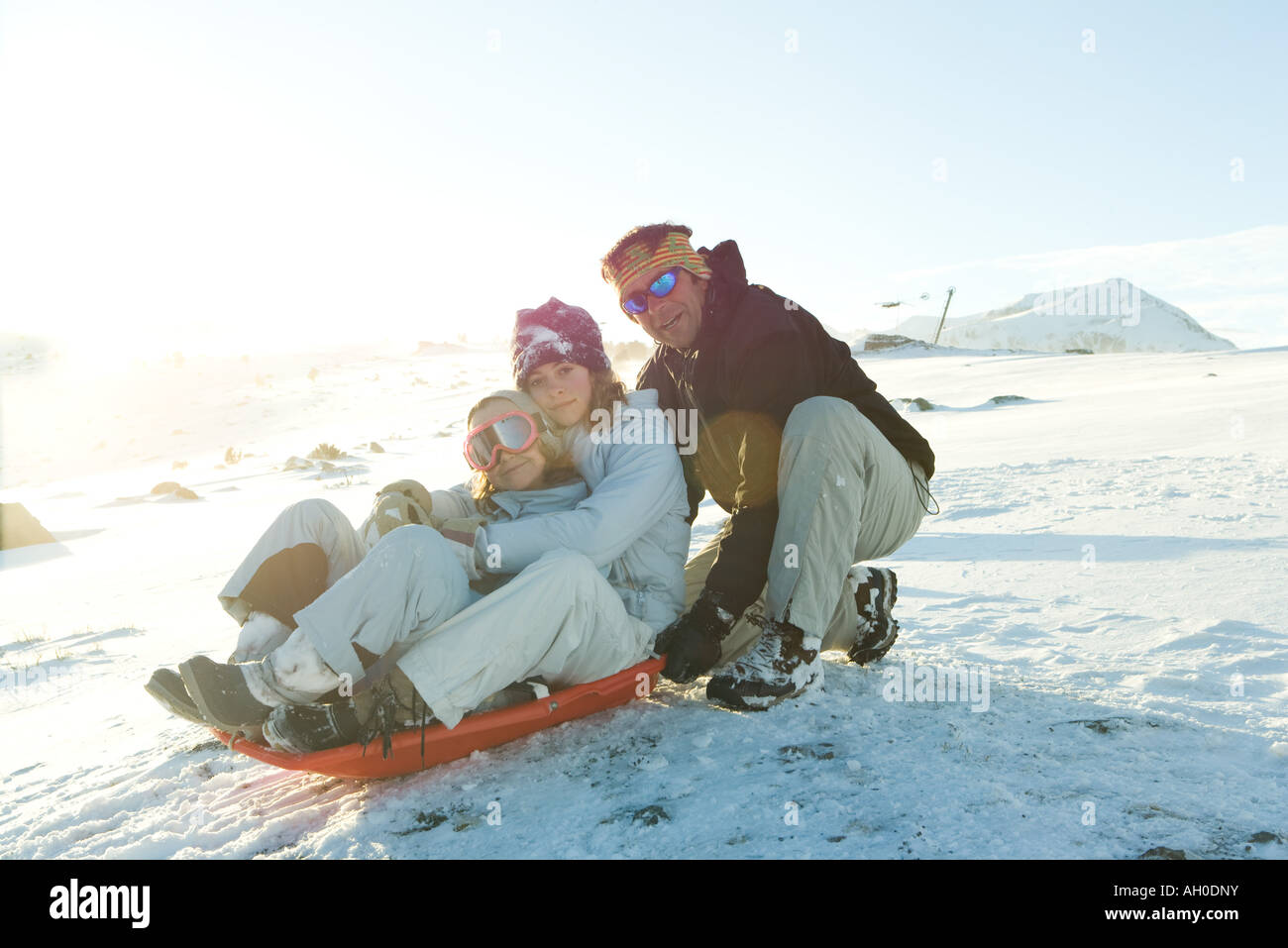 Mature man crouching behind sled with two daughters, smiling at camera ...
