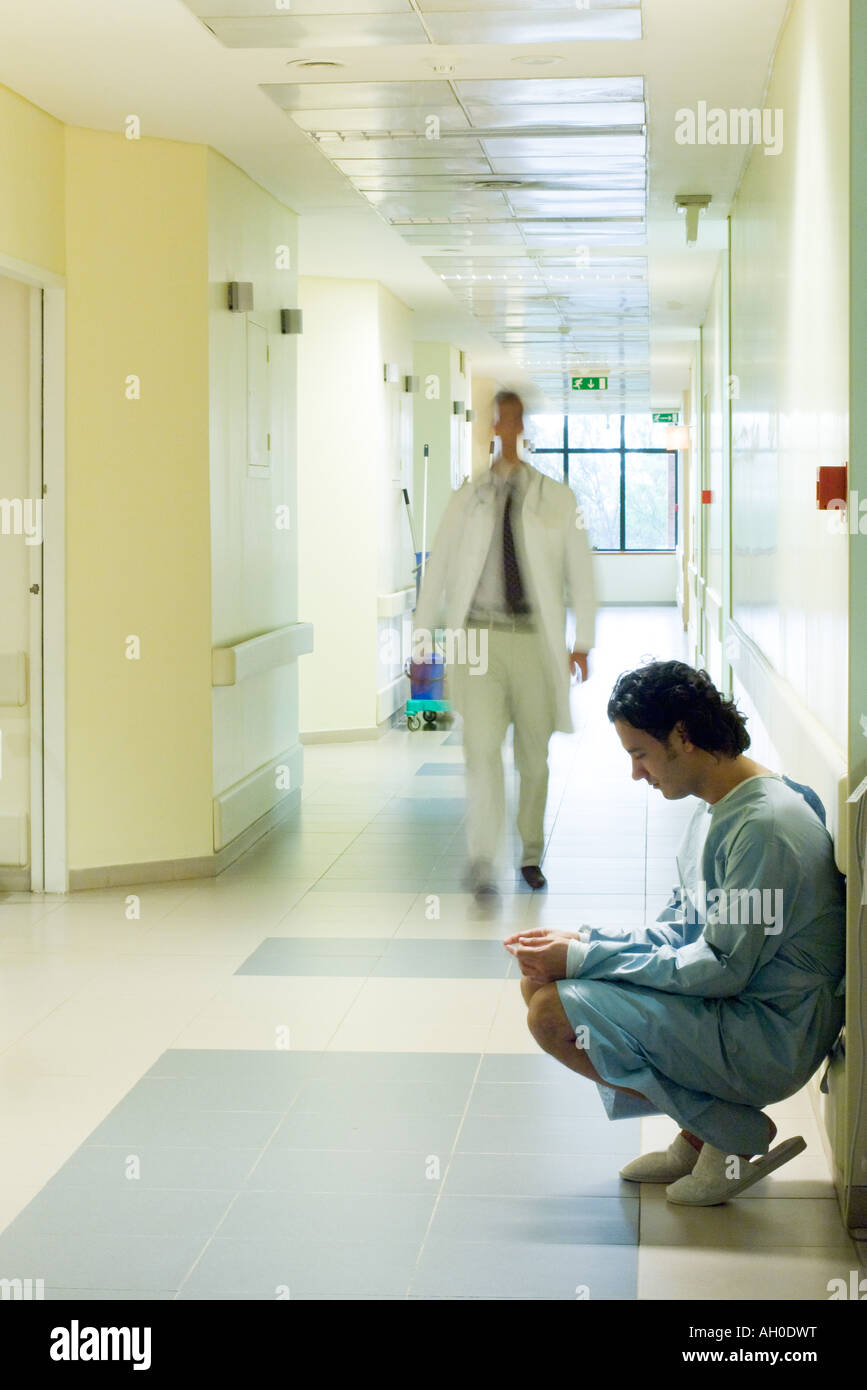 Male patient crouching in hospital corridor, looking down, doctor ...
