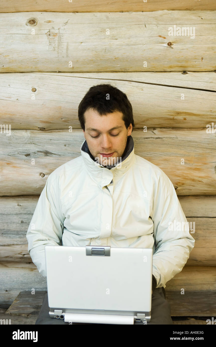 Young man using laptop next to log cabin Stock Photo - Alamy