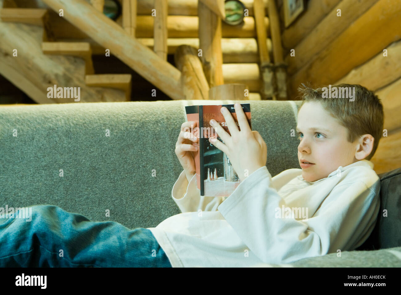Boy reclining on couch, reading book Stock Photo - Alamy