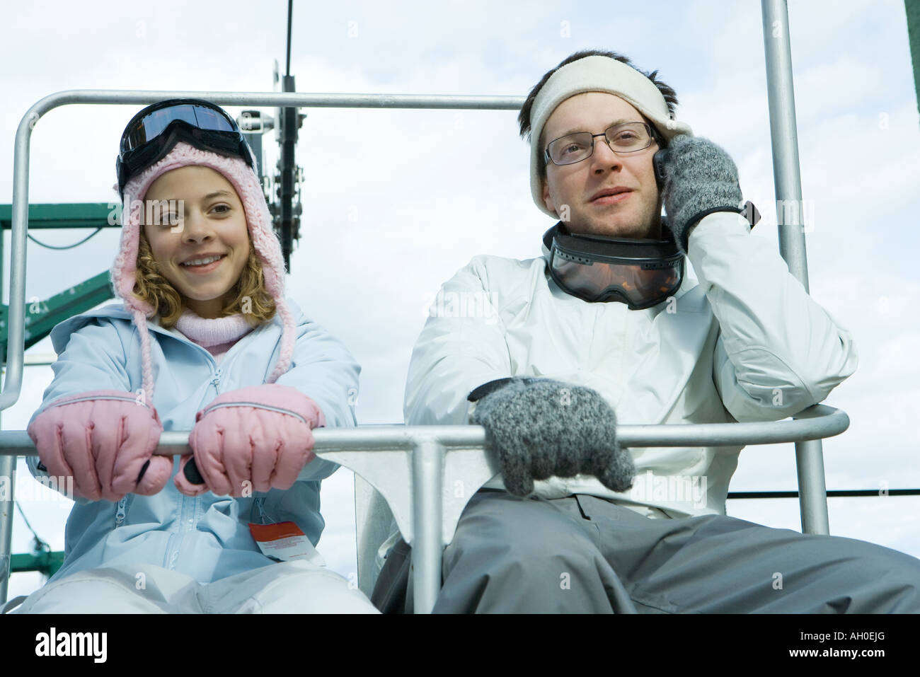 Young man using cell phone, sitting on chair lift with sister, both ...