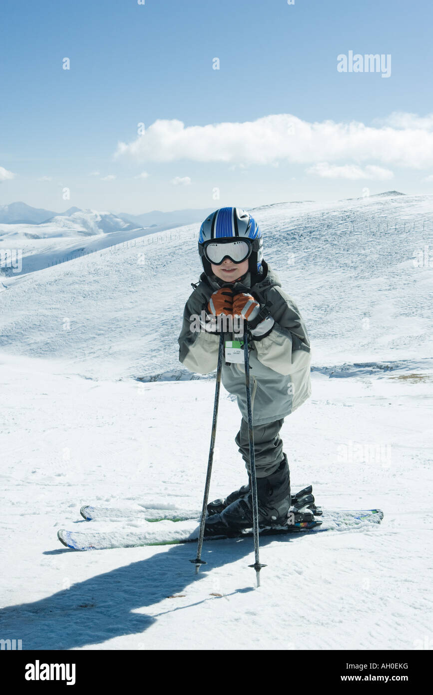 Young skier leaning on ski sticks, smiling at camera, full length ...