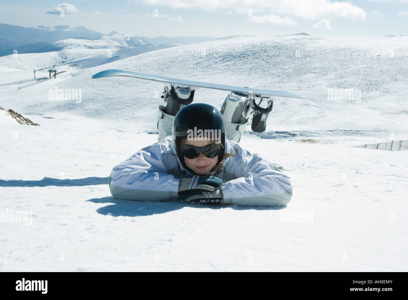 Young snowboarder lying on the ground, head resting on arms, smiling at ...