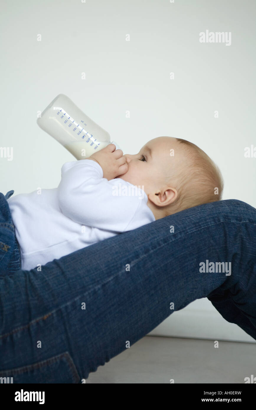 Baby reclining on lap, drinking milk from bottle, side view Stock Photo ...