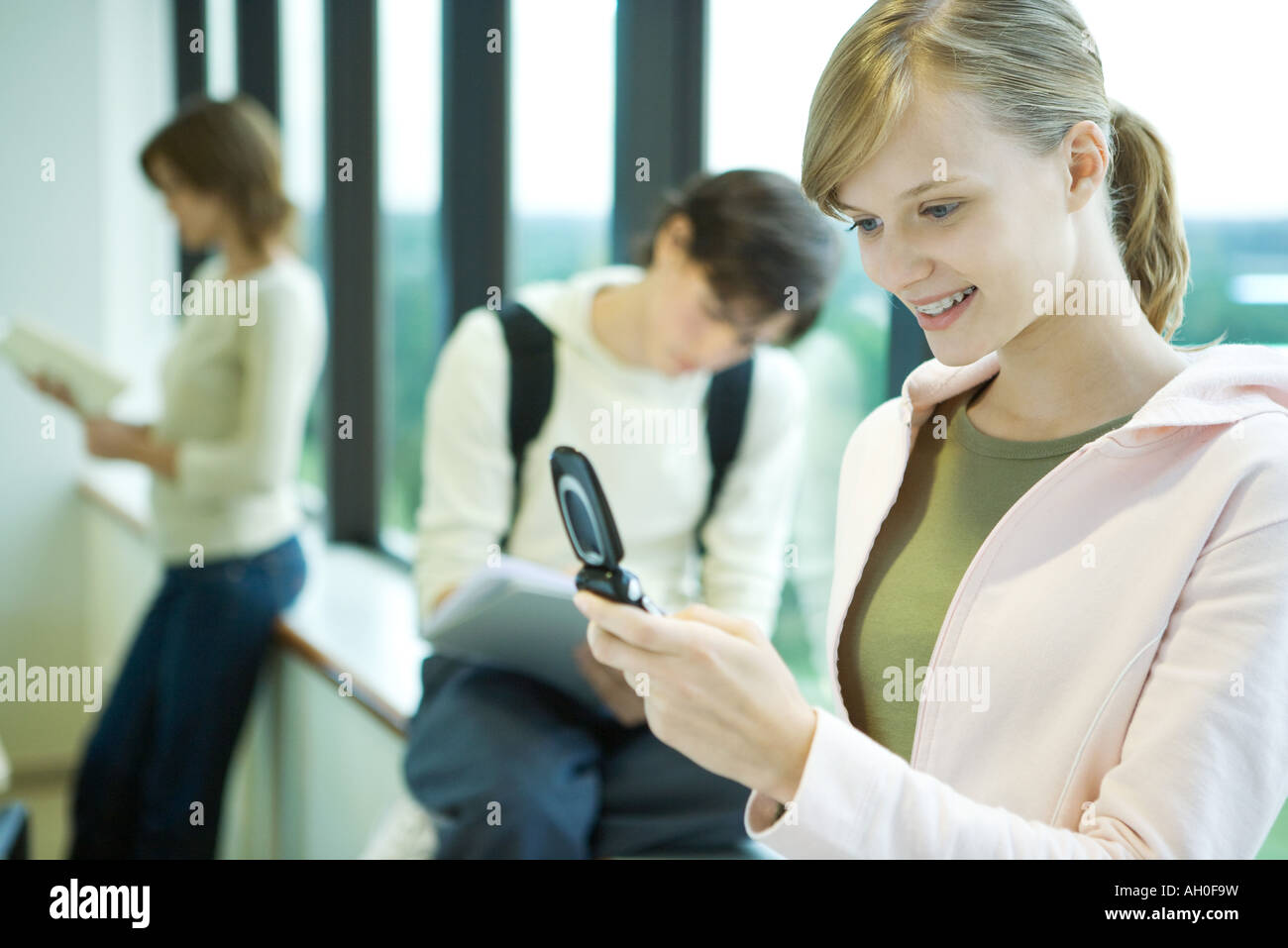 Female student looking at cell phone in front of window, smiling ...