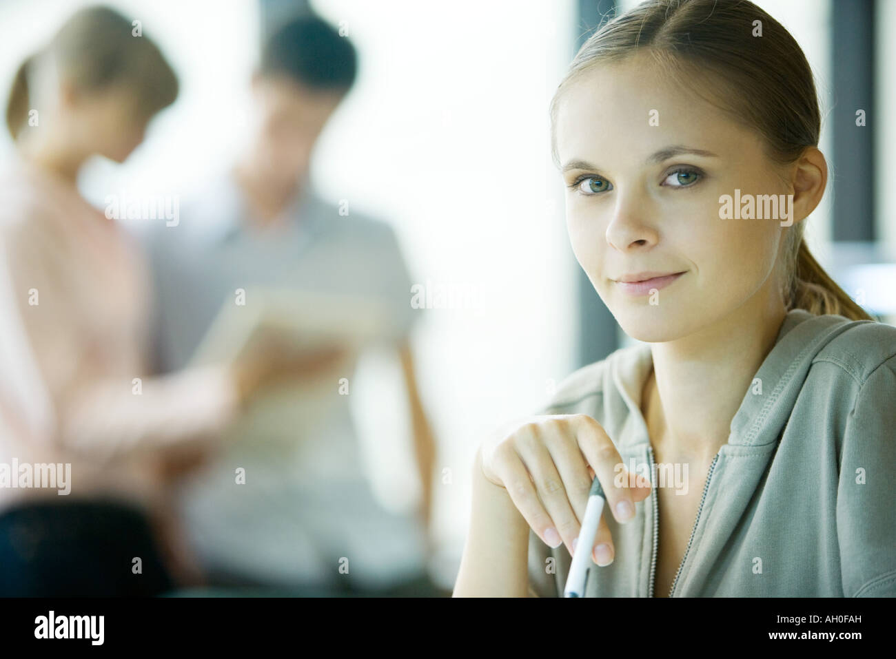 Young woman holding pen, smiling at camera Stock Photo - Alamy