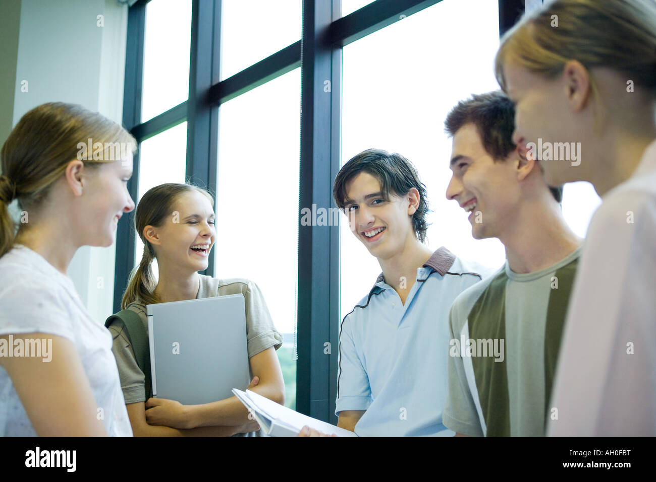 Group of students standing in front of window, smiling, one looking at ...