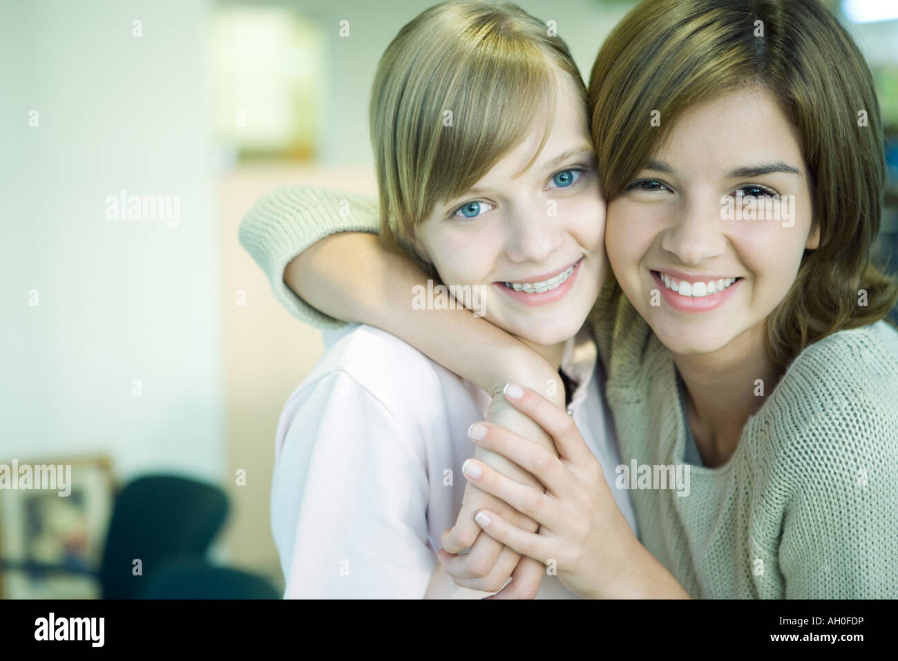 Two young friends smiling at camera, cheek to cheek, one's arm around ...