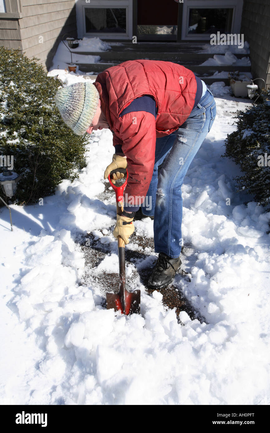 Man bent over using a garden spade to clear front walkway of house ...