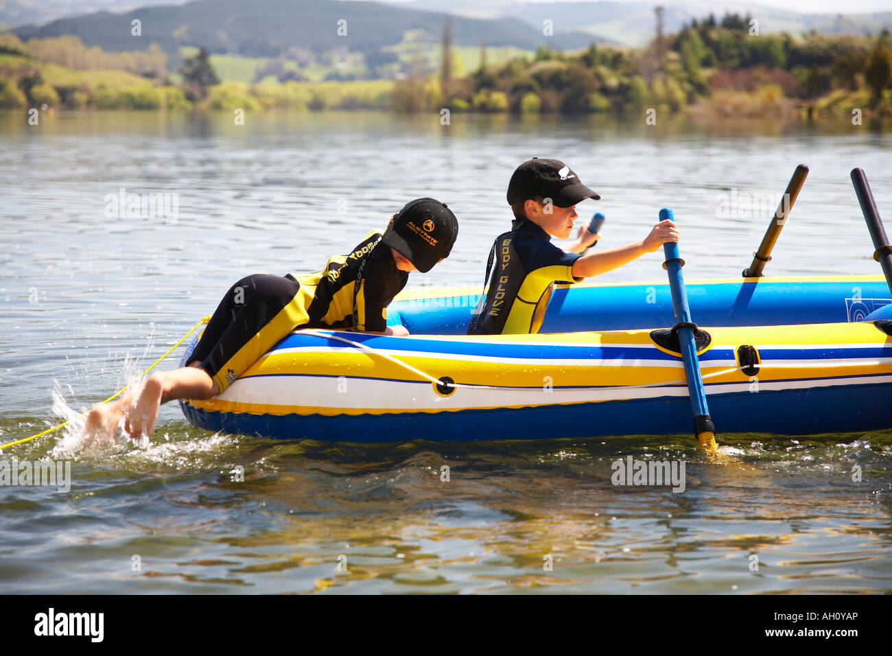 two boys 6 wearing wetsuits playing in an inflatable boat on lake Stock ...