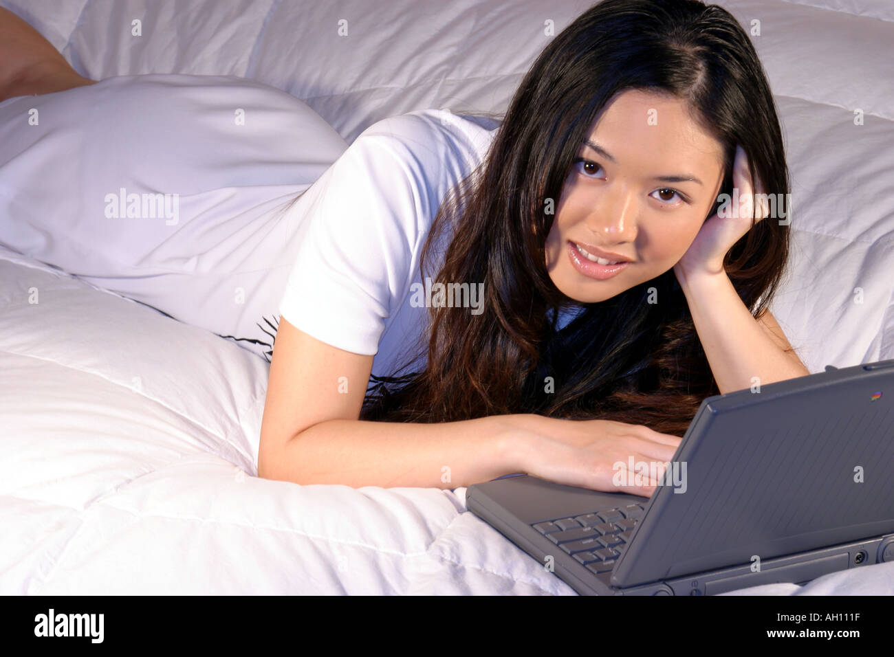 Woman lying down on bed working on a laptop Stock Photo - Alamy