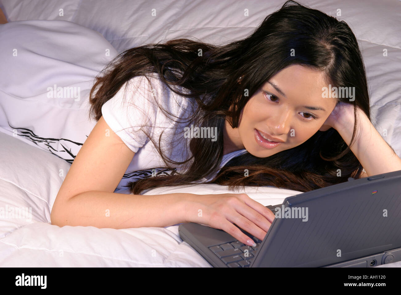 Woman lying down on bed working on a laptop Stock Photo - Alamy