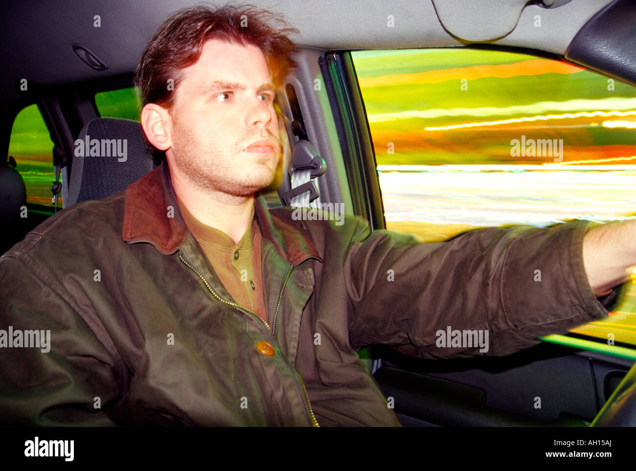 Young man driving through the city at night, lights blurred behind him ...