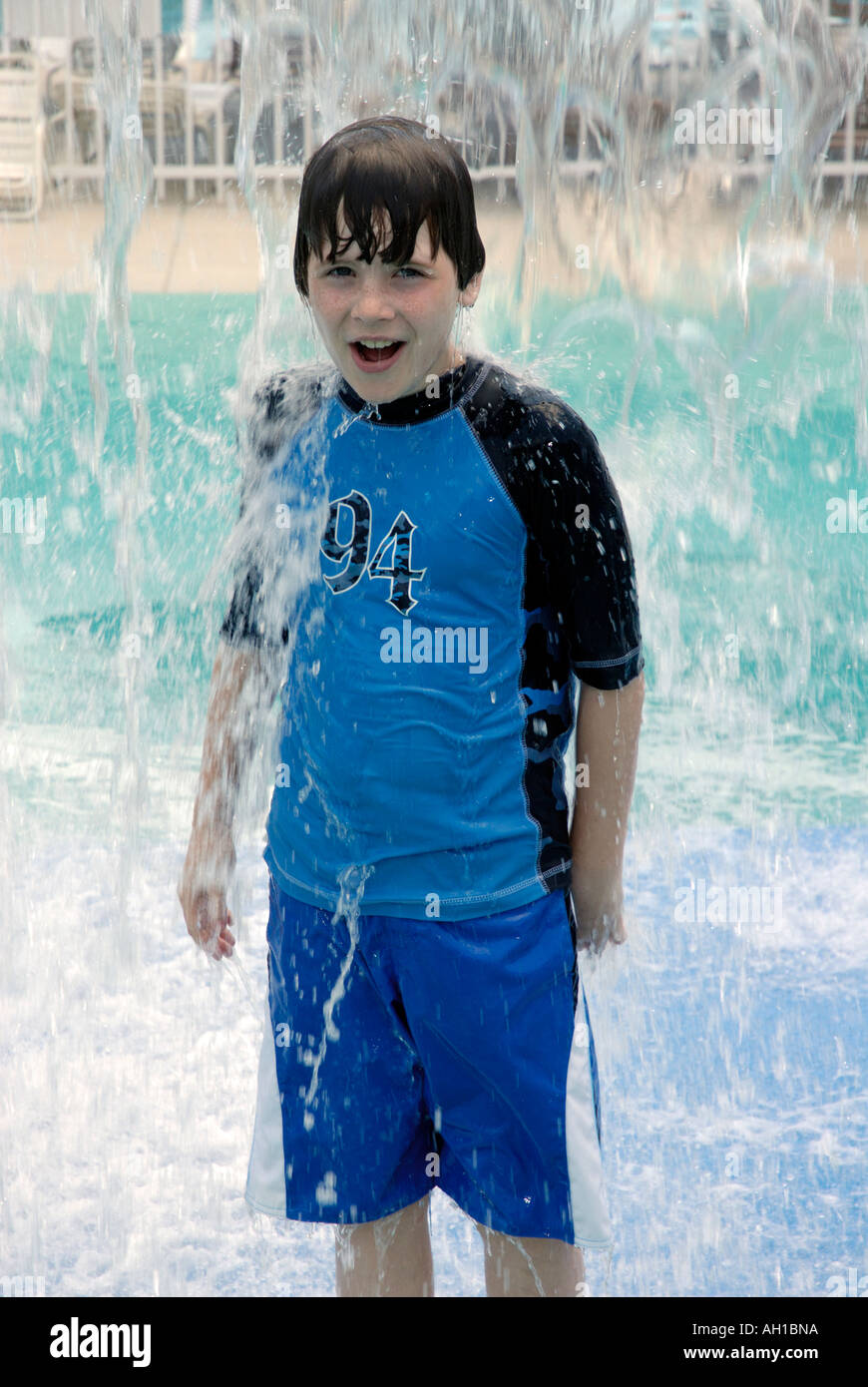 Young boy smiling in water fall waterfall cooling off at playground in ...