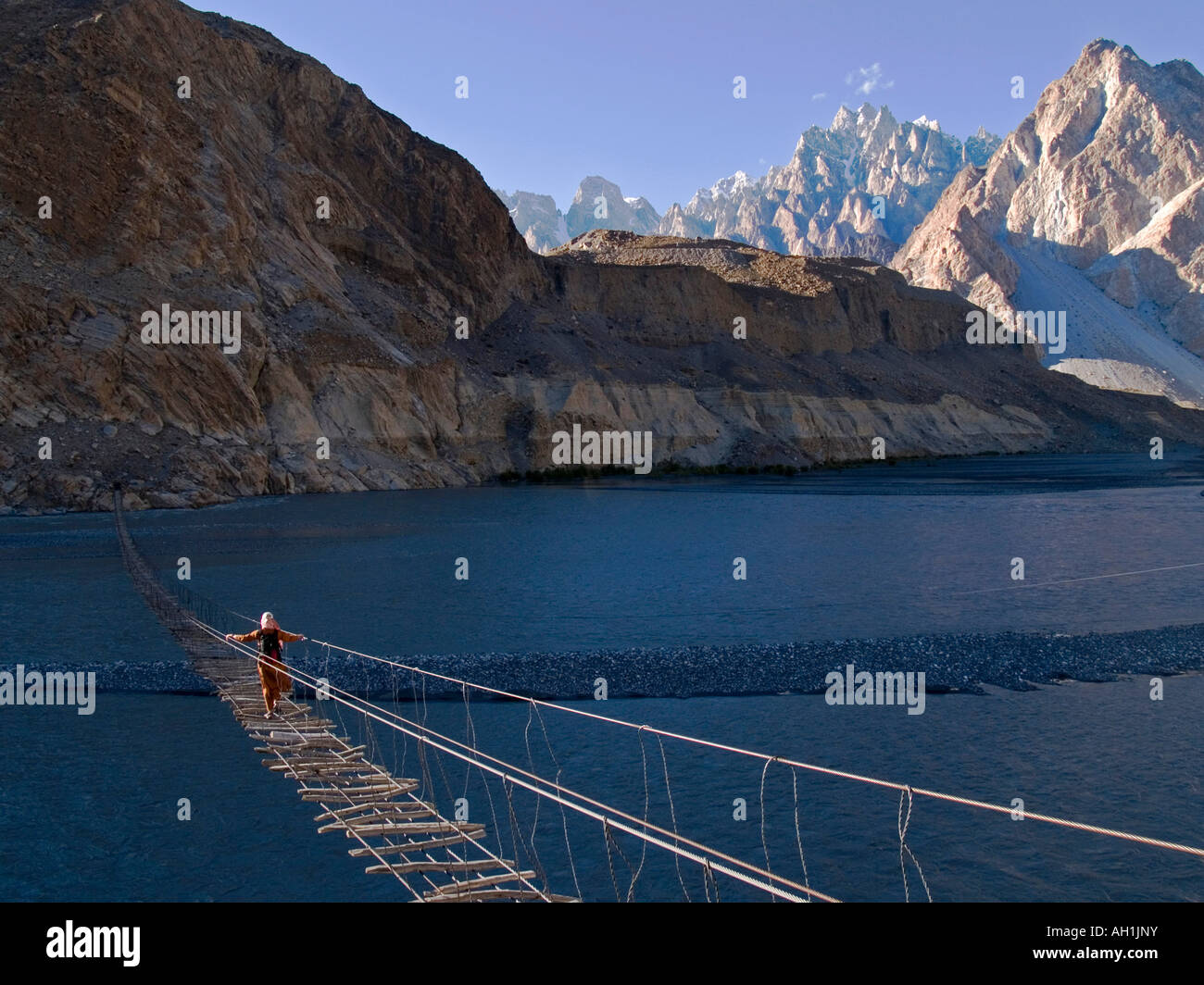 trekker makes an intrepid footbridge crossing of the Hunza River in the ...