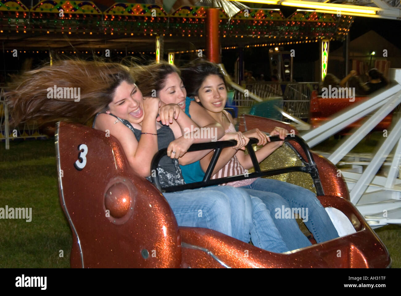 Three girlfriends on nighttime carnival ride having fun Stock Photo - Alamy