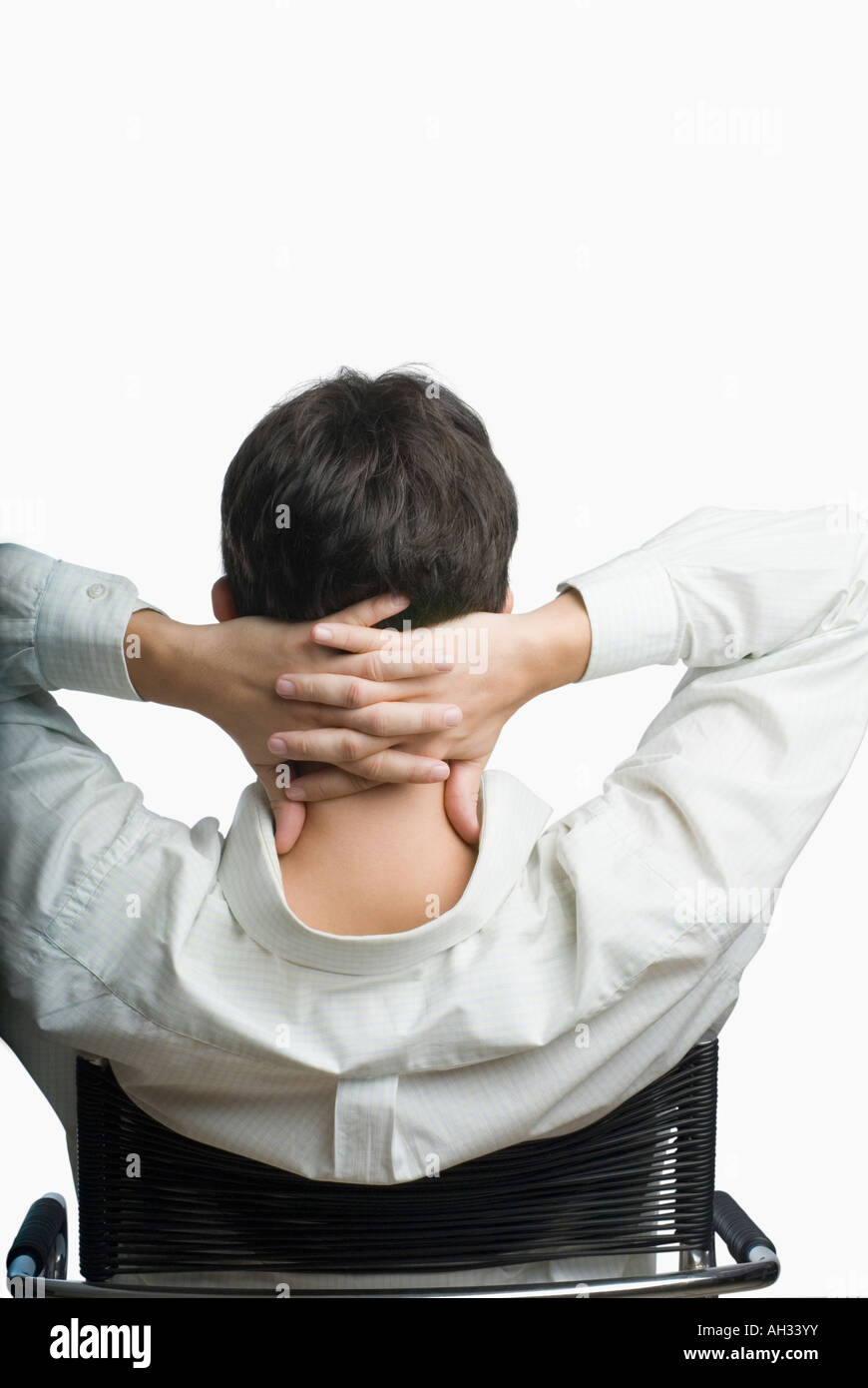 Rear view of a young man sitting on an armchair with his hands behind ...